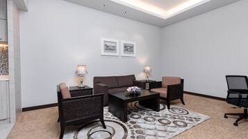 Quarto moderno com sofá, duas poltronas, mesa de centro e tapete. Há duas luminárias em mesas laterais e duas quadros na parede.