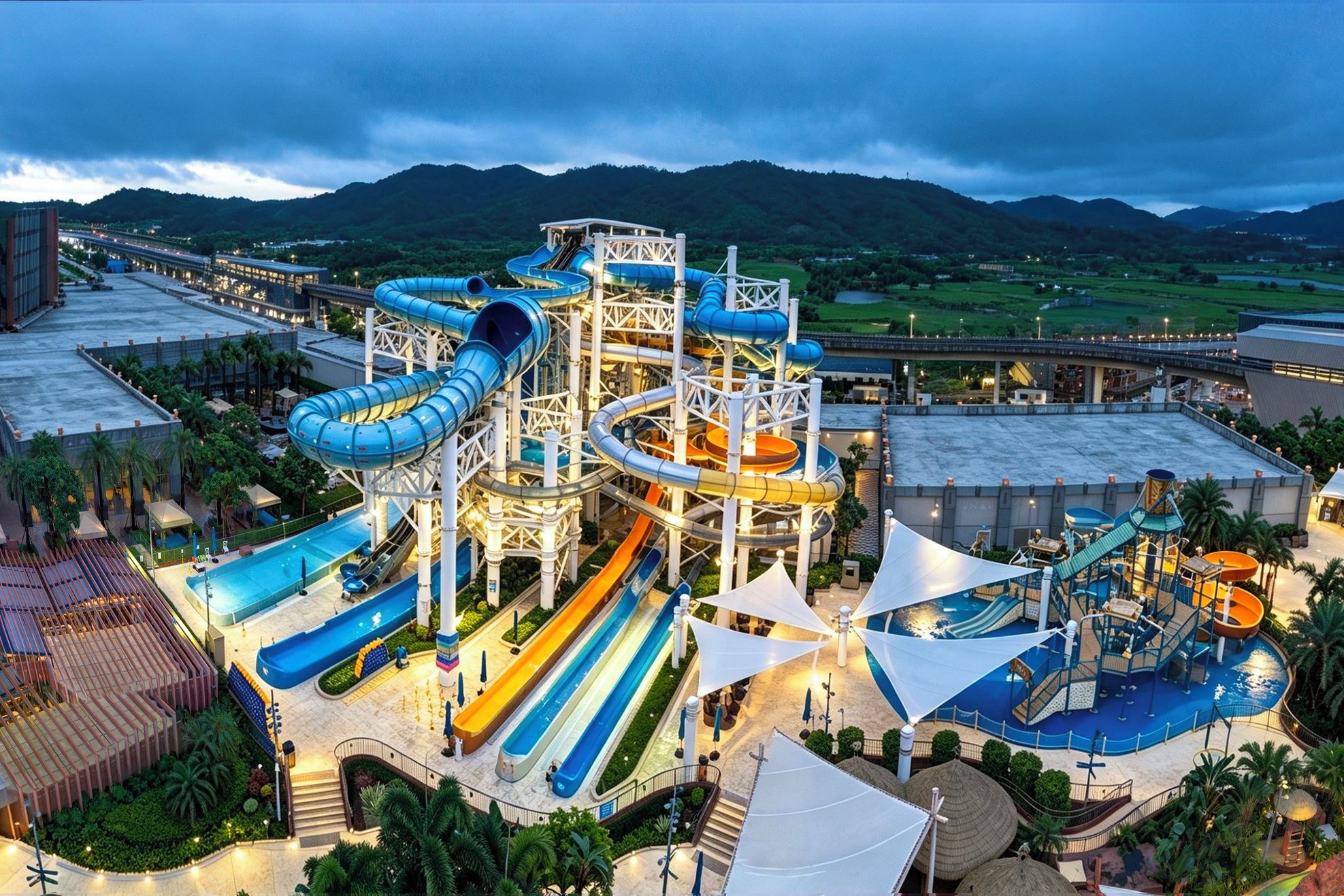 Parque aquático com diversas piscinas e toboáguas, cercado por vegetação e colinas.