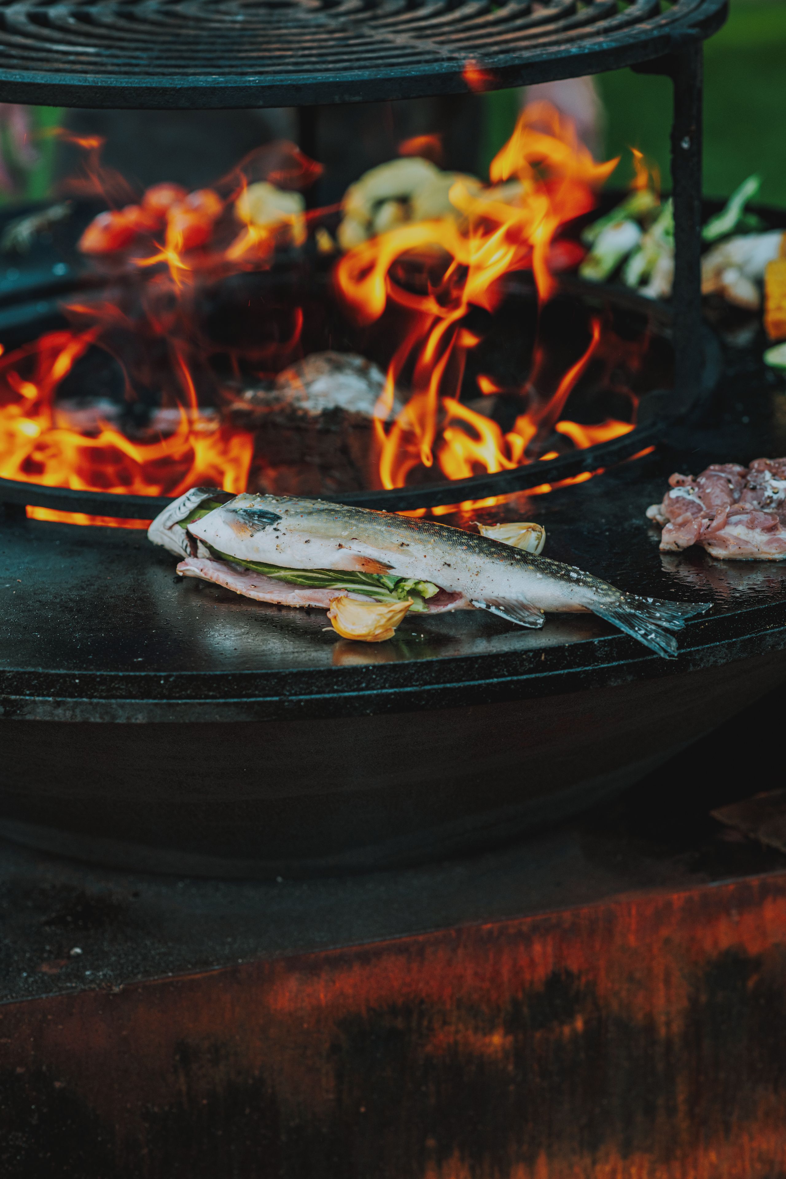 Uma grelha com peixe e carne a ser assada sobre chama aberta.