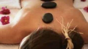 Uma pessoa recebendo massagem nas costas com pedras e uma toalha.