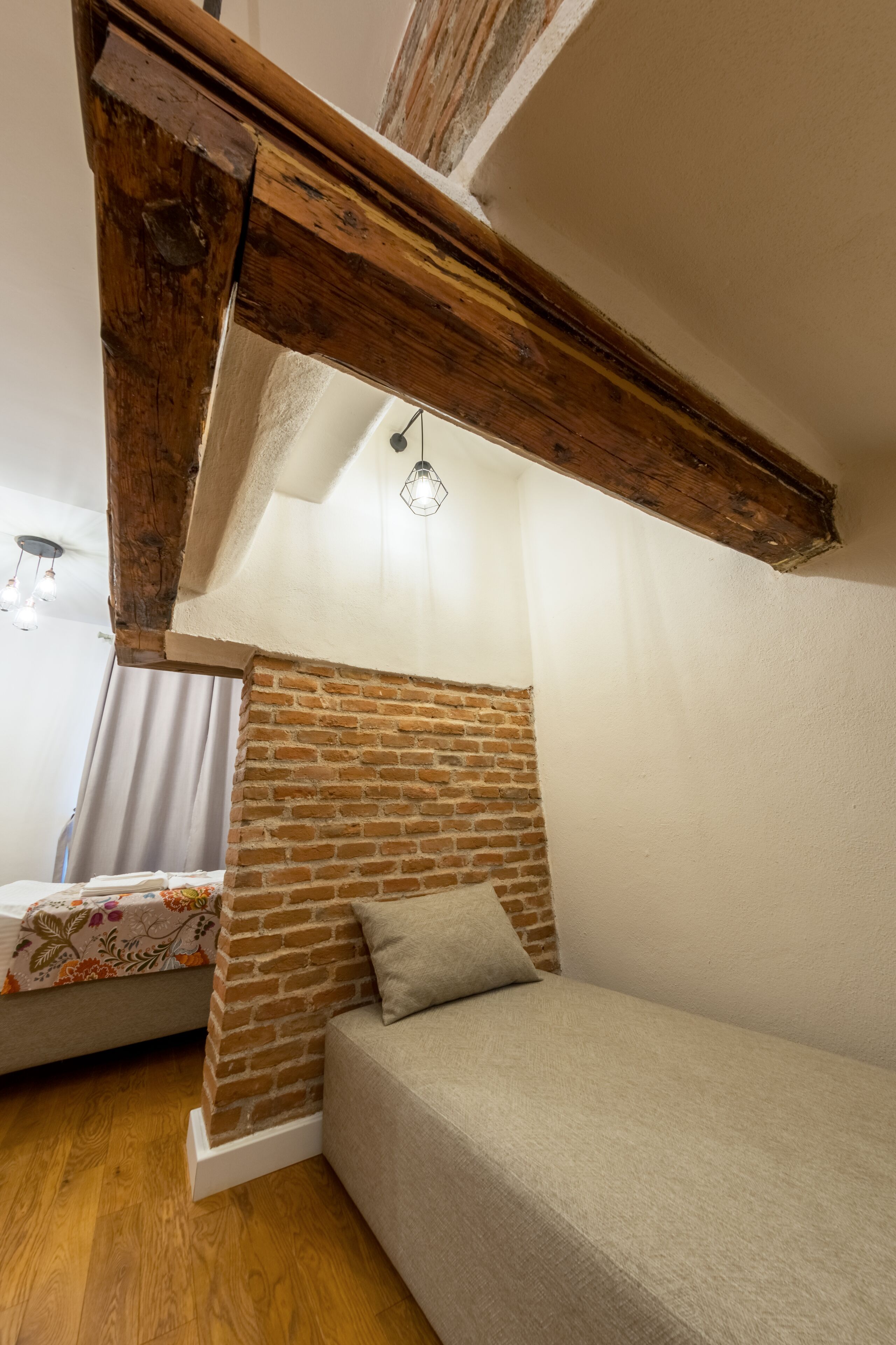 Um quarto aconchegante com parede de tijolos, teto com vigas de madeira, uma cama e um lustre pendurado.