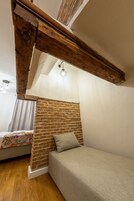 Um quarto aconchegante com parede de tijolos, teto com vigas de madeira, uma cama e um lustre pendurado.