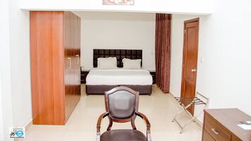 Quarto de hotel com cama, guarda-roupa de madeira, escrivaninha e uma cadeira.