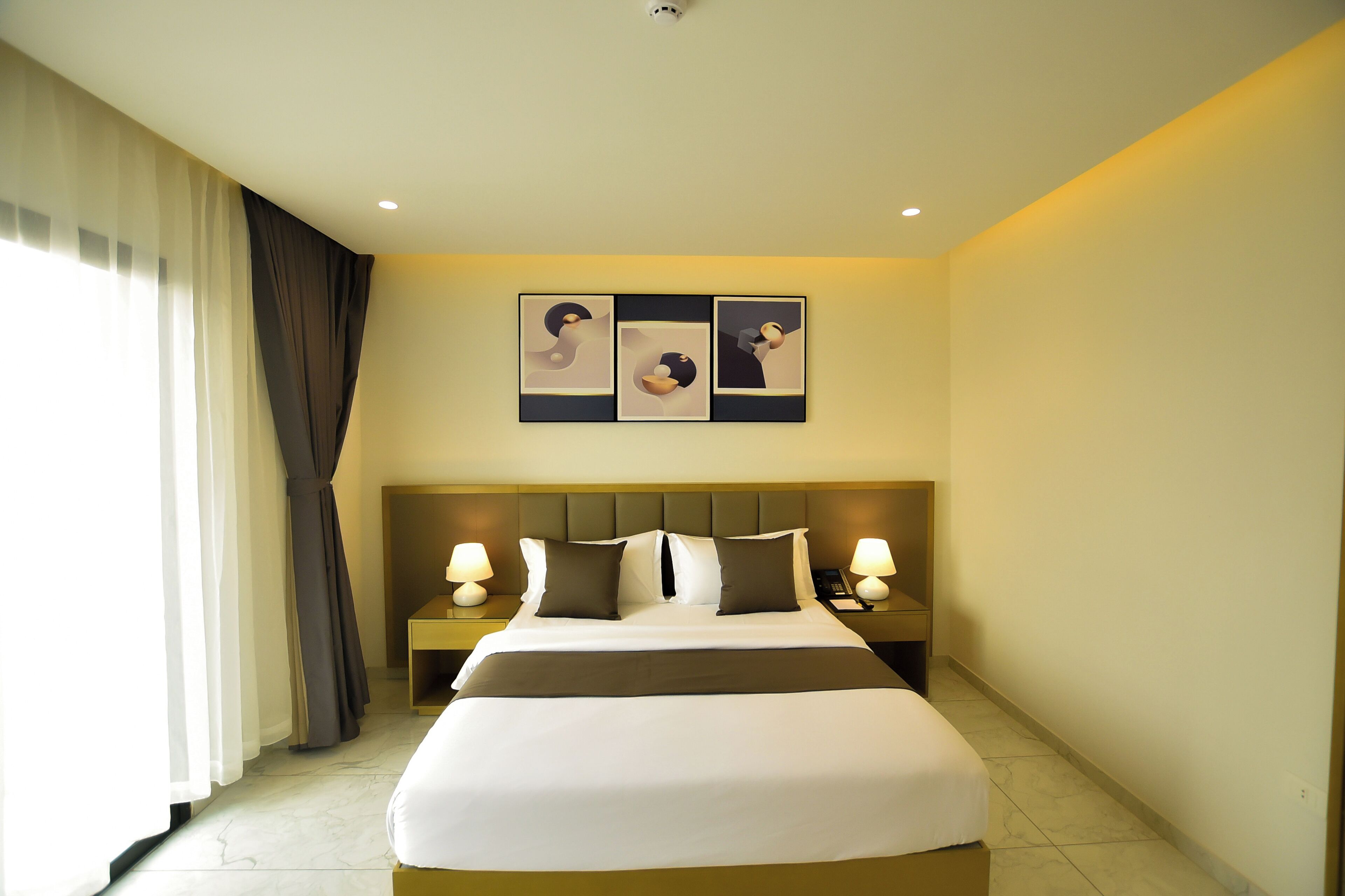 Quarto de hotel com uma cama grande, duas mesas de cabeceira com abajures, uma cabeceira e três obras de arte emolduradas na parede.