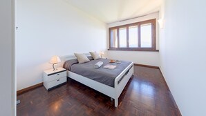 Quarto com cama, mesa de cabeceira, abajur e janela com vista.