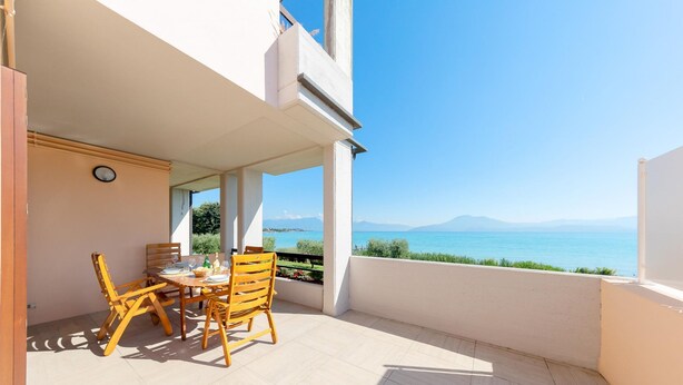 Uma varanda com mesa e cadeiras, oferecendo uma vista panorâmica do mar e das montanhas.