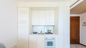 Uma cozinha compacta com armários brancos, forno embutido, fogão a gás e pia.
