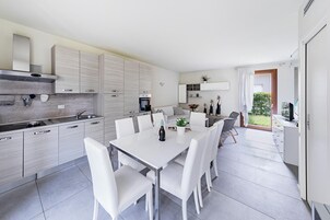 Uma cozinha moderna com armários brancos, uma mesa de jantar com cadeiras e um forno embutido.