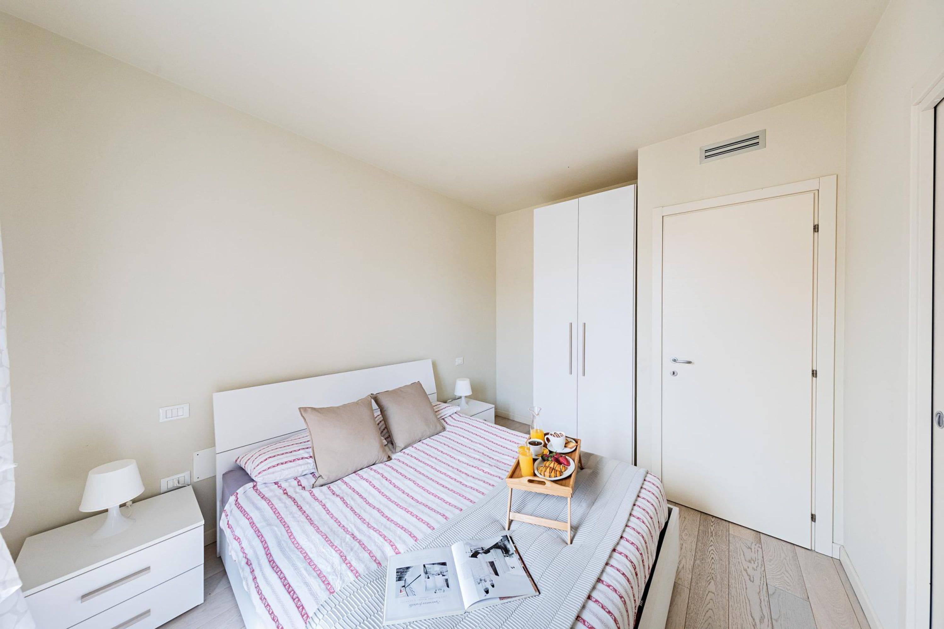 Quarto com cama, mesa de cabeceira, guarda-roupa e bandeja com itens de café da manhã.