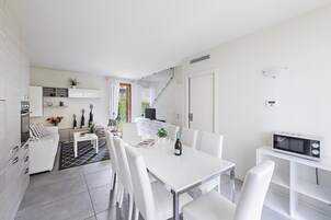Cozinha moderna com armários brancos, área de refeições com mesa e cadeiras brancas, e micro-ondas embutido.