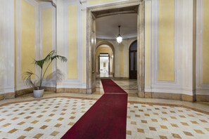 Um corredor com carpete vermelho, paredes brancas e padrão de piso xadrez.