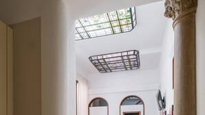 Um interior espaçoso com teto alto, área de jantar com cadeiras de madeira, uma coluna grande e uma janela de vitrais.