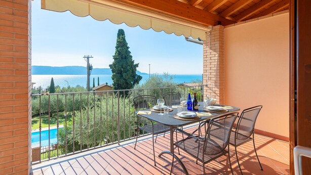 Varanda com mesa posta para refeições, vista para uma piscina e paisagem cénica do mar e montanhas.