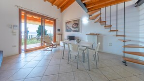 Ampla sala de estar com teto de madeira, mesa de jantar com cadeiras, escada e uma grande janela com vista para o exterior.