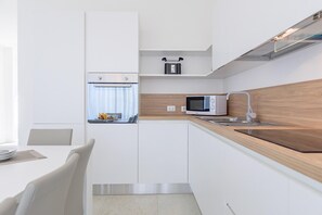 Uma cozinha moderna com armários brancos, bancada de madeira, micro-ondas embutido e uma janela com cortinas.