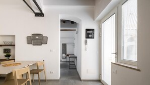 Cozinha moderna com mesa de jantar, cadeiras e bancada. Há um corredor que leva a um banheiro.