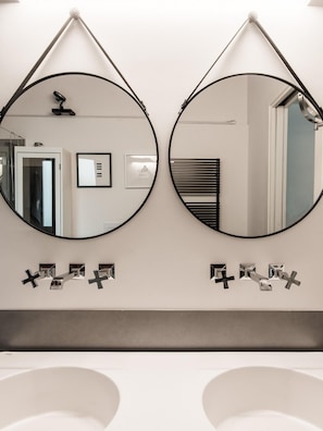 Dois espelhos fixados na parede com design moderno, um porta-toalhas e um quadro emoldurado.