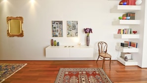 Uma sala de estar moderna com uma mesa consola branca, um espelho decorativo e uma estante com livros e objetos decorativos.