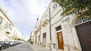 Uma rua de paralelepípedos ladeada por edifícios históricos, carros estacionados e um céu claro.