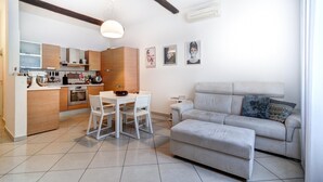 Uma cozinha moderna com armários brancos, uma mesa de jantar e um sofá numa sala de estar.