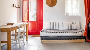 Quarto com mesa de madeira, cadeira branca, porta vermelha e cama com almofadas listradas.