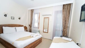 Quarto de hotel com cama de madeira, uma cama menor, um espelho, televisão e janela com cortinas.