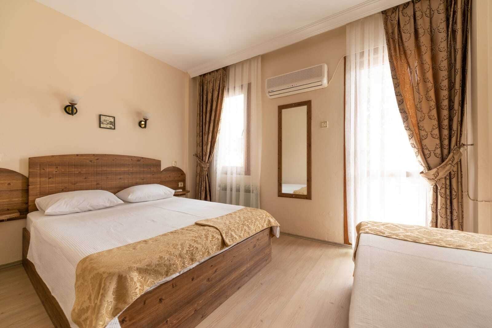 Quarto com cama de madeira, mesa de cabeceira, cadeira, espelho grande e janela com cortinas.