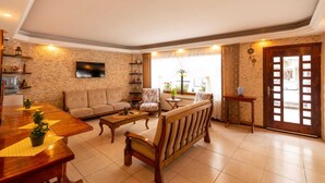Uma sala de estar com sofá, poltrona, mesa de centro e televisão na parede.