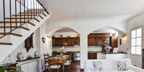 Uma sala de estar ampla com uma mesa de jantar, um sofá e uma escada que leva a um andar superior.