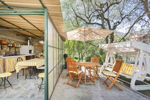 Um pátio externo com uma mesa, cadeiras, um banco de madeira e uma pérgula com cobertura.