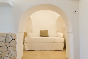 Um quarto acolhedor com parede de pedra, cama branca com almofadas e teto em arco.