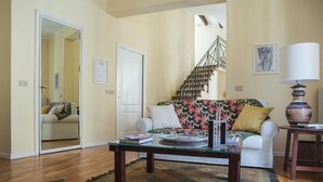 Uma sala de estar com um sofá, uma mesa de centro, um tapete, um abajur e uma escada.