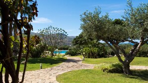 Uma trilha de pedra serpenteia por um jardim ajardinado, com árvores e vista para uma montanha ao longe.