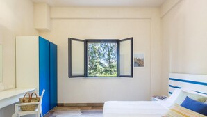 Quarto com cama, escrivaninha, cadeira, janela e vista para árvores.
