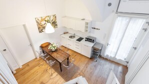 Uma cozinha compacta com armários brancos, uma mesa de jantar de madeira e uma luminária pendente.