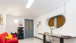 Uma sala de estar moderna com um sofá vermelho, uma mesa de centro de vidro e um espelho redondo na parede.