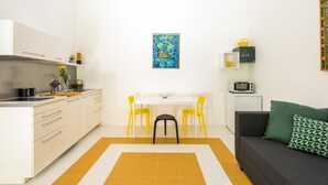 Cozinha compacta com mesa e cadeiras, micro-ondas e um sofá com almofada estampada.