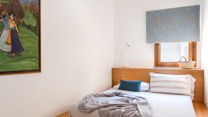 Quarto com cama, quadro, luminária e janela.