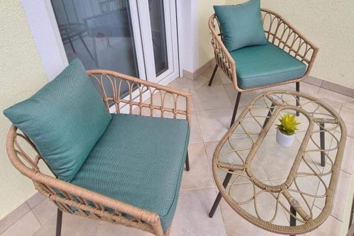 Uma varanda com mobiliário de vime, incluindo duas cadeiras e uma mesa pequena, e uma porta de correr de vidro.