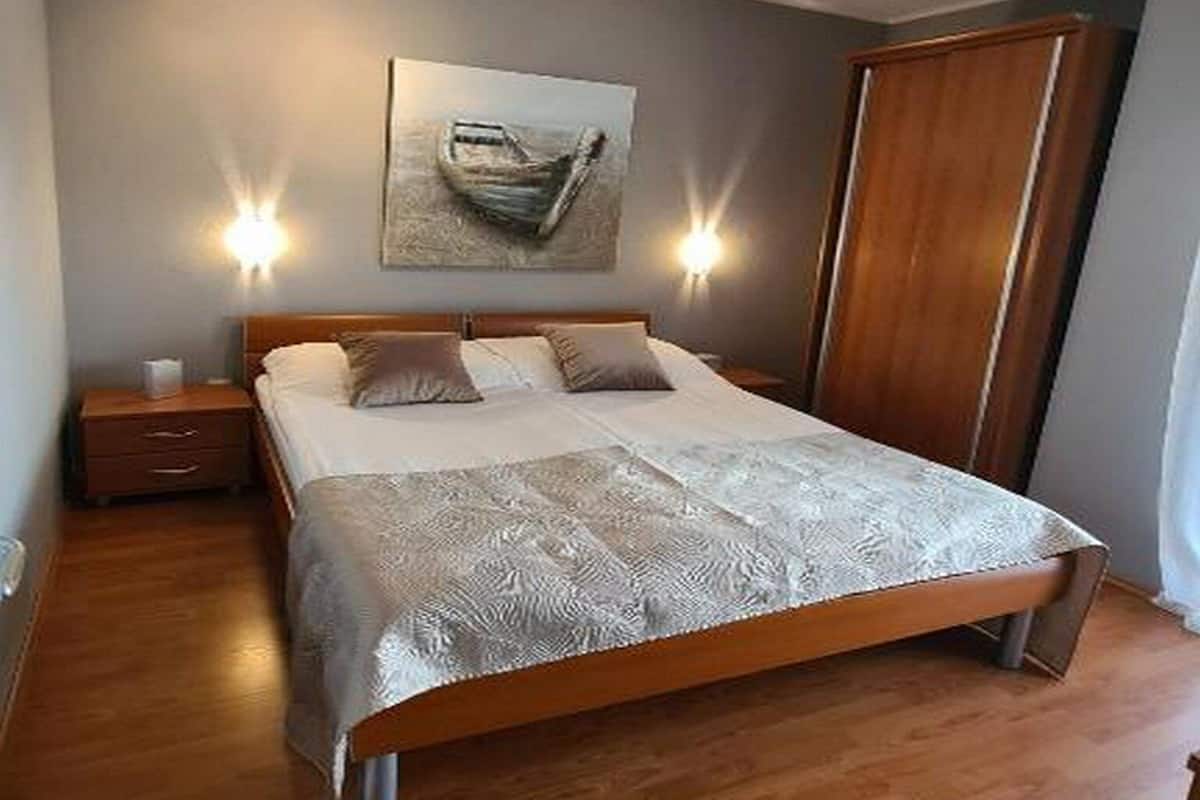 Um quarto com cama, mesa de cabeceira, guarda-roupa de madeira e luminária na parede.