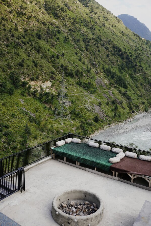Um terraço com lareira, área de estar acolchoada em tons de verde e vista para um rio e montanhas.