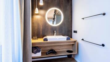 Uma casa de banho moderna com uma toucador de madeira, um espelho redondo com luz e um porta-toalhas.