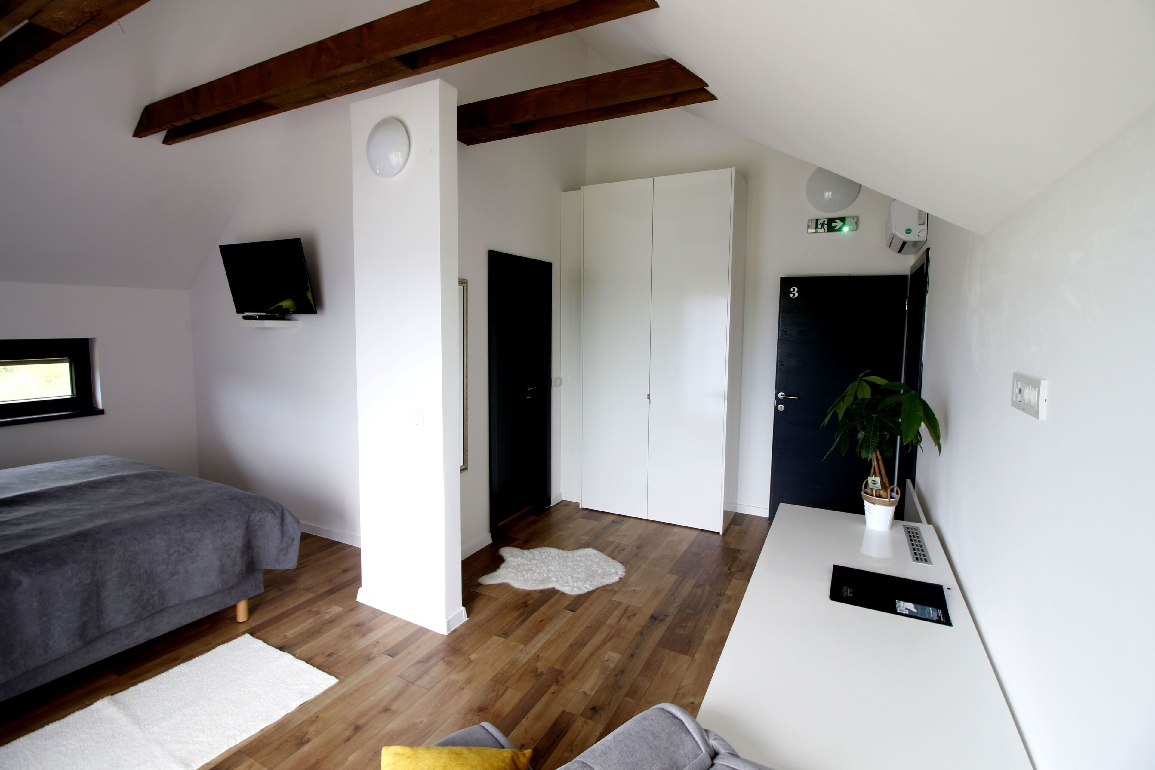 Quarto com cama, televisão, guarda-roupa branco, escrivaninha com planta e porta marcada com o número 3.