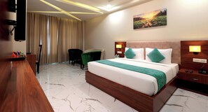 Quarto de hotel com uma cama, escrivaninha, cadeira, televisão e um quadro na parede.