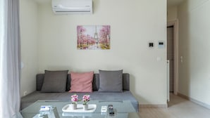 Uma sala de estar moderna com uma mesa de centro de vidro, um sofá com almofadas cinzas, um quadro da Torre Eiffel e um aparelho de ar condicionado na parede.
