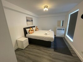 Quarto com cama, mesa de cabeceira, penteadeira e janela.