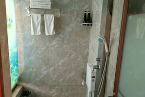 Casa de banho com soalho em mármore, um porta-toalhas com toalhas dobradas, chuveiro com esguicho manual e porta de vidro.