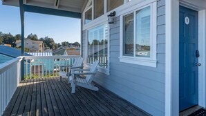Um deck de madeira com duas cadeiras Adirondack brancas, uma porta azul e um corrimão branco.