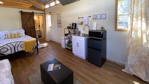 Quarto compacto e bem iluminado, com cama, pequeno espaço de cozinha, teto de madeira e janela com cortinas.
