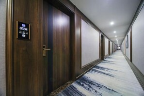 Corredor de hotel com portas de madeira, piso coberto por carpete e uma placa indicando a sala número 8568.